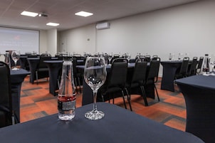 Uma sala de conferências com mesas preparadas para uma reunião, cada uma com uma garrafa e uma taça de vinho.