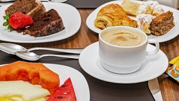 Mesa posta com pratos de comida, uma chávena de café e talheres.