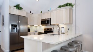 Uma cozinha moderna com armários brancos, eletrodomésticos de aço inoxidável e uma ilha central com banquetas.