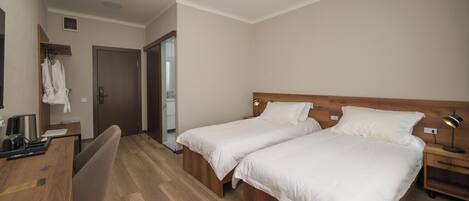 Quarto de hotel com duas camas, uma escrivaninha, uma cadeira, um guarda-roupa e um banheiro visível por uma porta aberta.