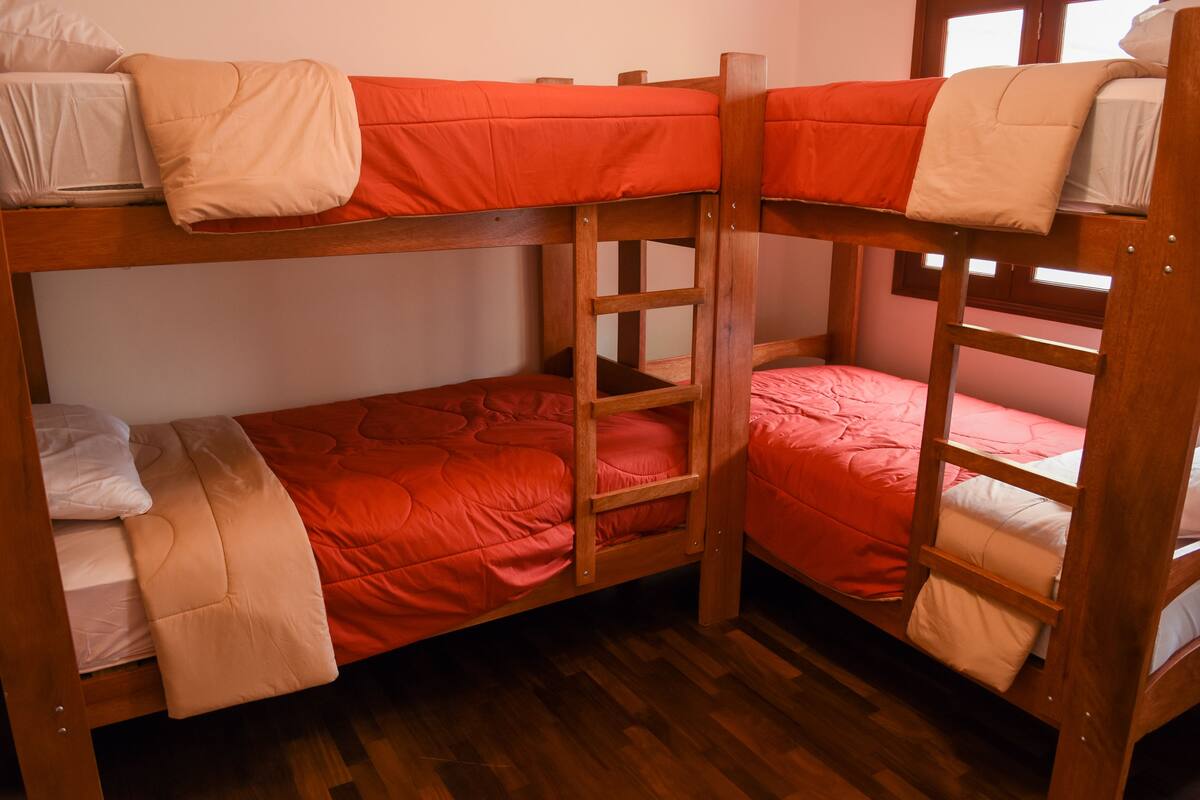 Quarto com beliche de madeira, roupa de cama vermelha e almofadas brancas.