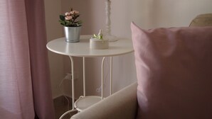 Quarto com uma mesa redonda branca, uma luminária, um vaso de planta e uma almofada rosa.