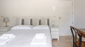 Quarto de hotel com uma cama grande, duas mesas de cabeceira, uma escrivaninha e uma porta.