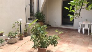 Um pátio com plantas em vasos, uma mesa branca com cadeiras e piso de azulejos.