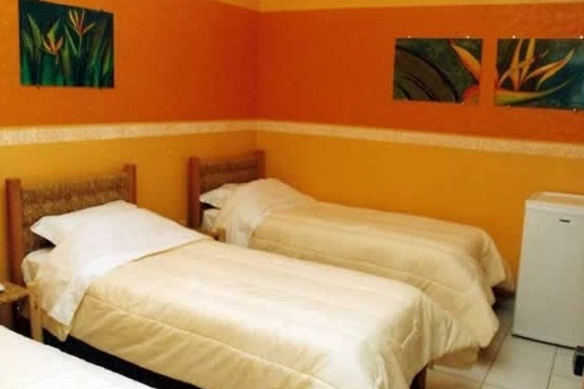 Quarto com duas camas, um refrigerador branco compacto e duas pinturas penduradas na parede.