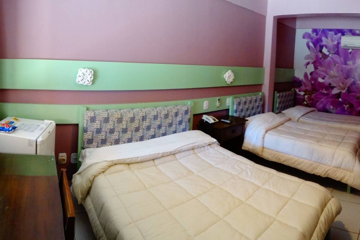 Quarto de hotel com duas camas, uma escrivaninha com computador e parede com um mural floral.