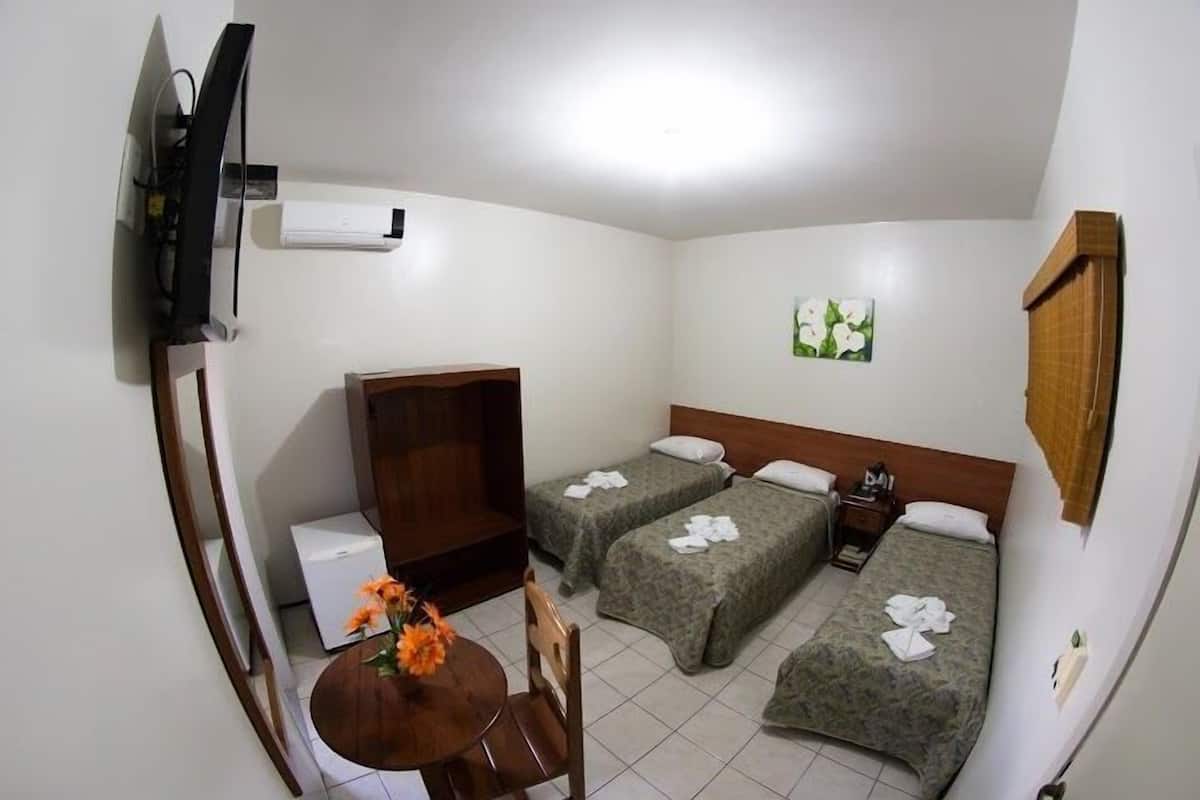 Quarto de hotel com duas camas de solteiro, uma escrivaninha de madeira com cadeira, televisão e uma mesinha com flores.