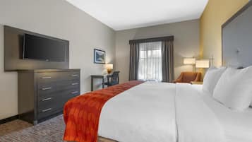 Quarto de hotel com uma cama grande, televisão de tela plana na parede, escrivaninha com cadeira e janela com cortinas.