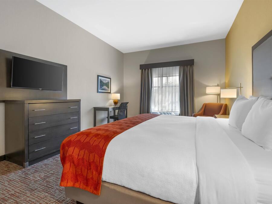 Quarto de hotel com uma cama grande, televisão de tela plana na parede, escrivaninha com cadeira e janela com cortinas.