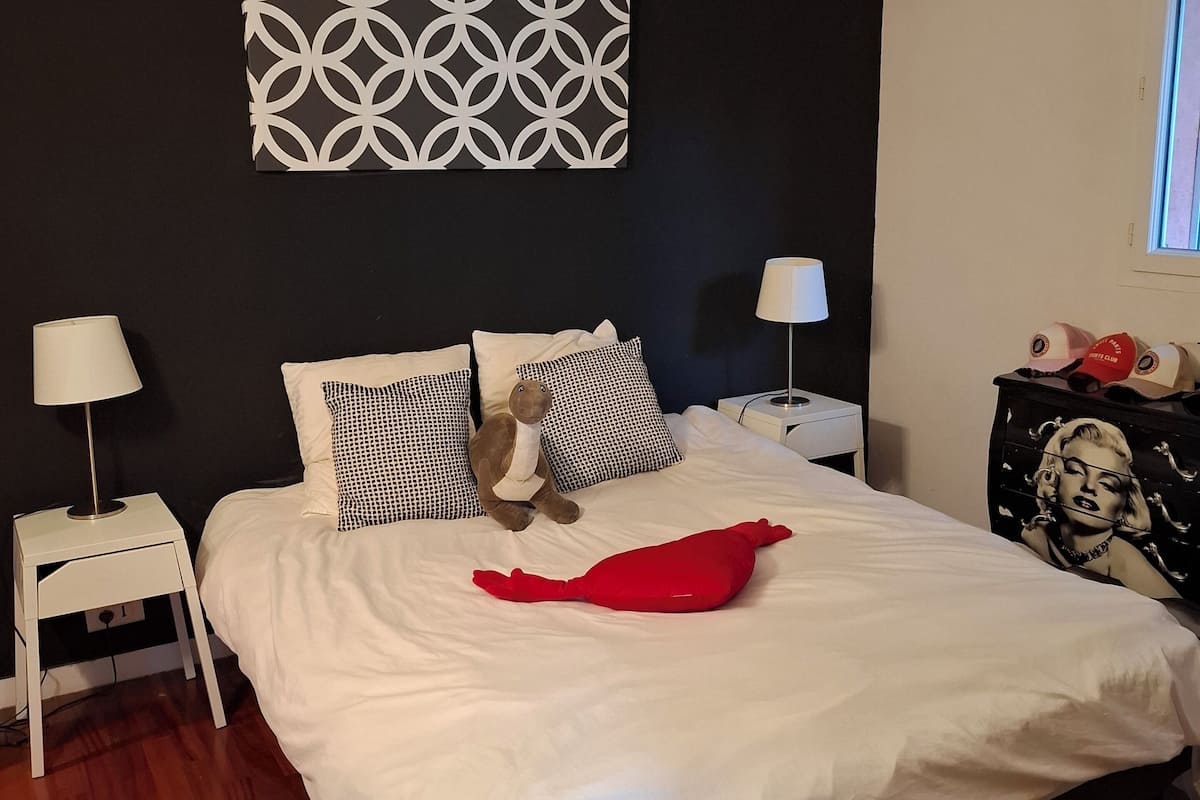 Quarto com cama, duas mesas de cabeceira, uma obra de arte na parede e uma janela.