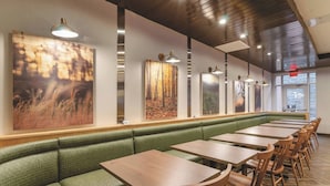 Um restaurante com um longo banco estofado verde, mesas de madeira e obras de arte nas paredes.