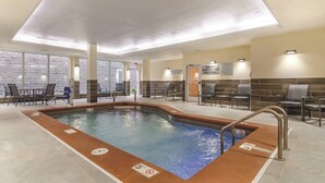 Piscina interior com água cristalina, rodeada por espreguiçadeiras e um chão em mosaico.