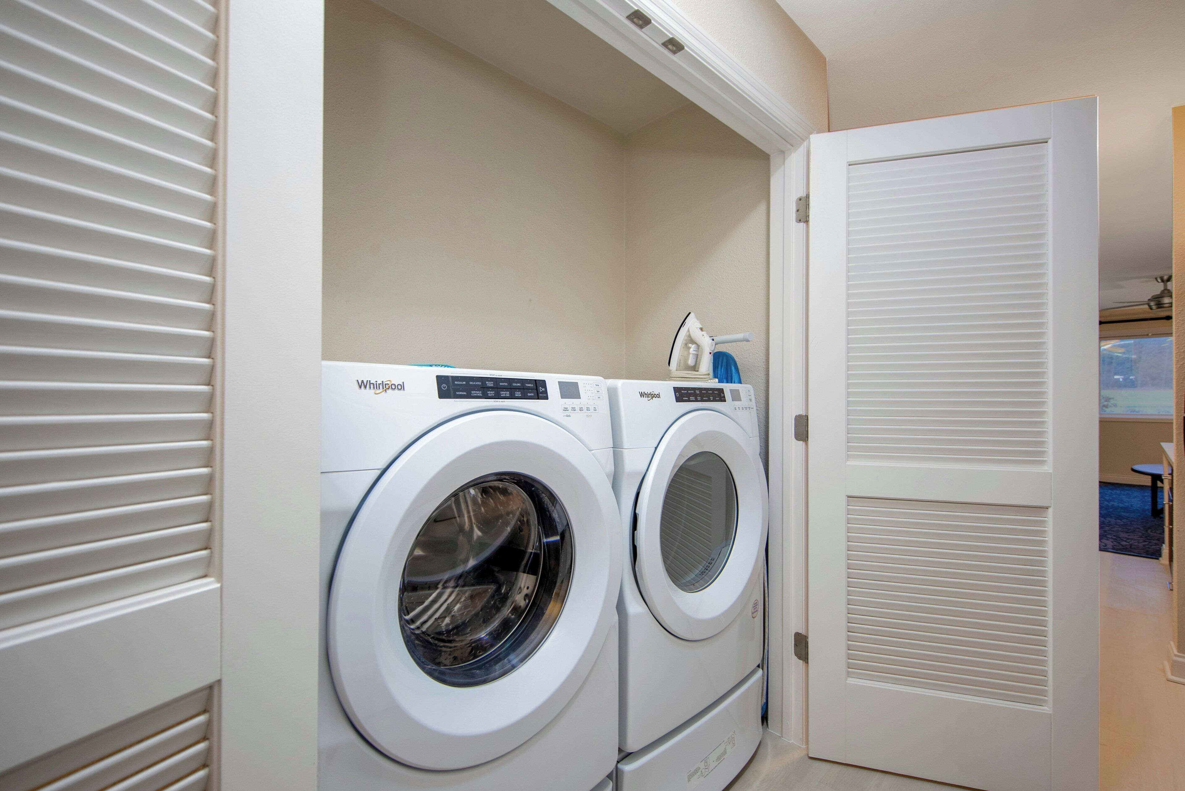 Uma lavanderia compacta com duas máquinas de lavar Whirlpool de abertura frontal, uma porta branca e uma janela com persianas.