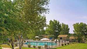 Piscina cercada por uma grade, com cadeiras de descanso e guarda-sóis, e um edifício ao fundo.