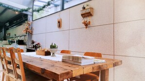 Uma mesa de jantar de madeira com cadeiras, toalha de mesa branca e uma tigela com plantas verdes.