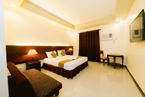Quarto de hotel com cama, mesa de cabeceira, luminária, cadeira e uma pequena mesa.