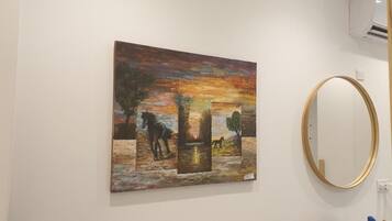 Casa de banho com uma grande pintura de uma cena de pôr do sol, um espelho redondo e artigos de higiene pessoal no balcão.