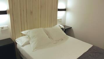 Cama bem arrumada com roupa de cama e almofadas brancas, um telefone ao lado da cama e cabeceira de madeira.