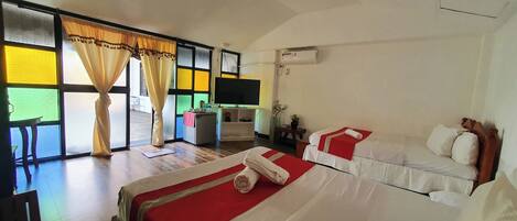 Quarto de hotel com uma cama grande, televisão, escrivaninha e vista para o exterior.