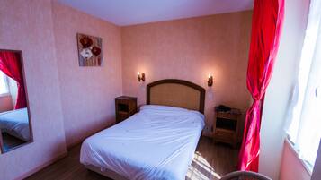 Quarto com cama, mesas de cabeceira, espelho e janela com cortinas vermelhas.