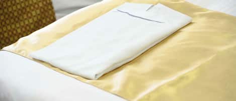 Cama bem arrumada com lençol branco e toalha dobrada em dourado.