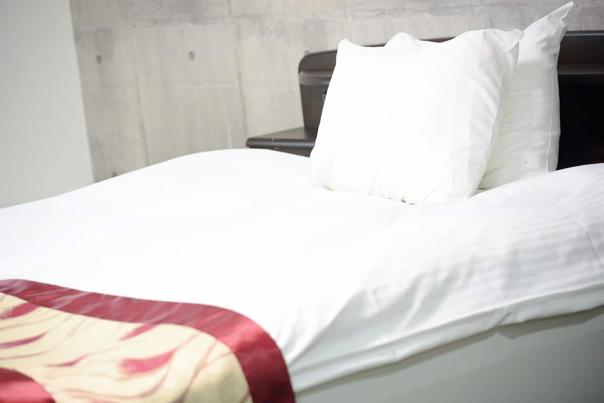 Cama bem arrumada com lençóis brancos e manta vermelha e bege.