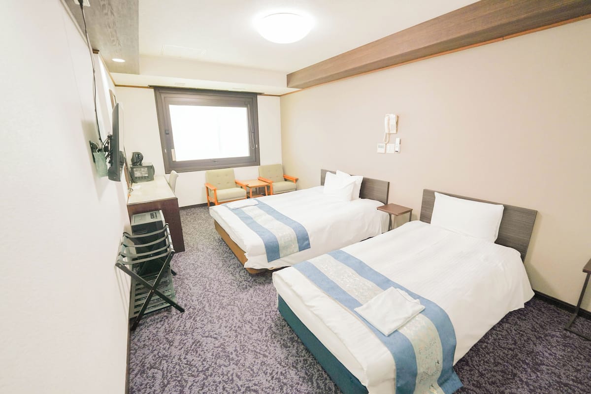 Quarto de hotel com duas camas, uma escrivaninha, uma cadeira, uma janela e uma televisão de tela plana.