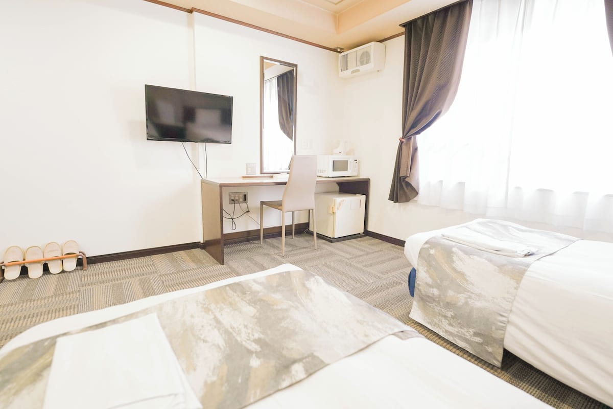 Quarto de hotel com cama, escrivaninha, cadeira, televisão, micro-ondas e sapateira.