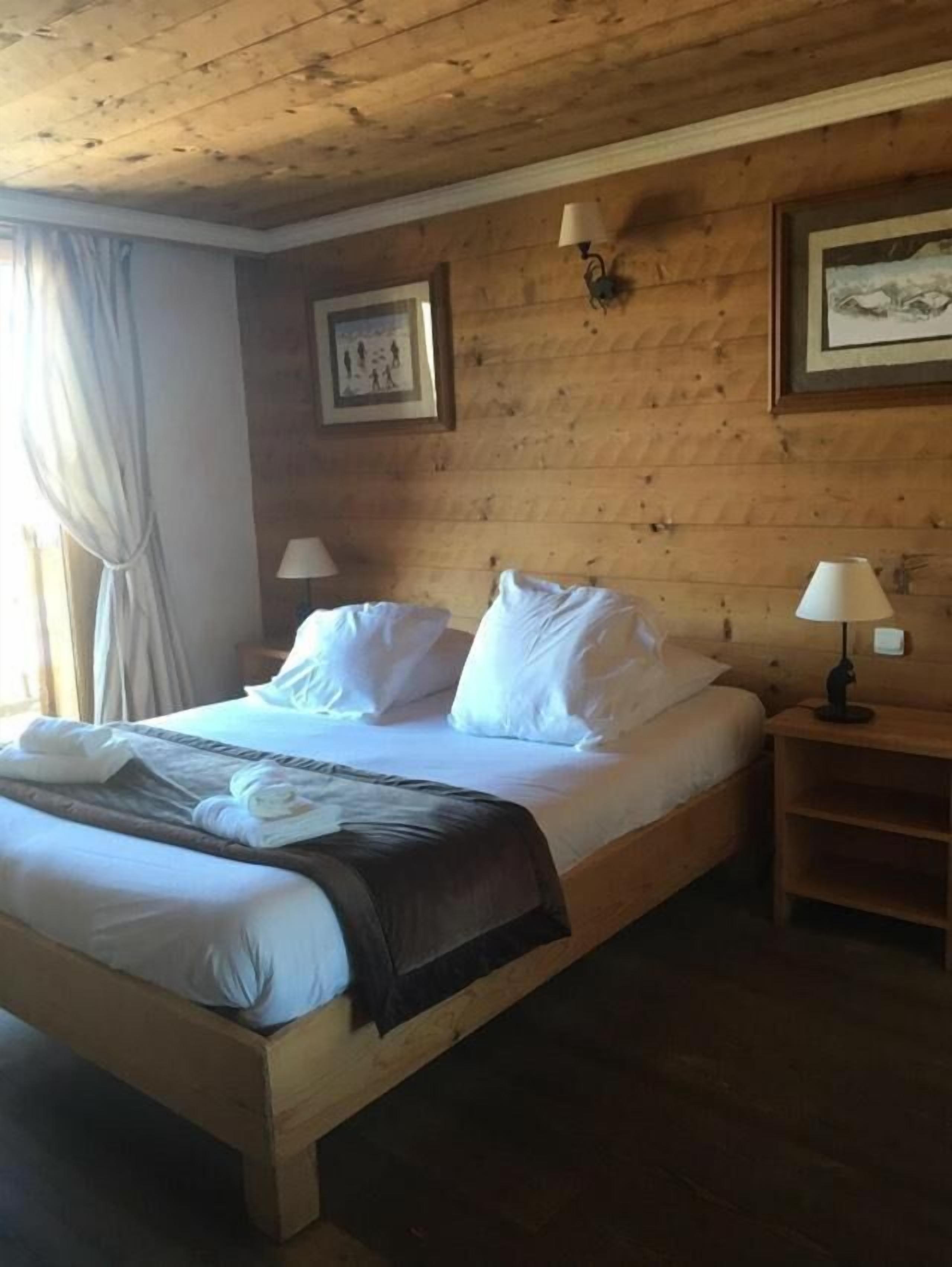 Um quarto com painéis de madeira, uma cama, duas luminárias de cabeceira e um quadro na parede.