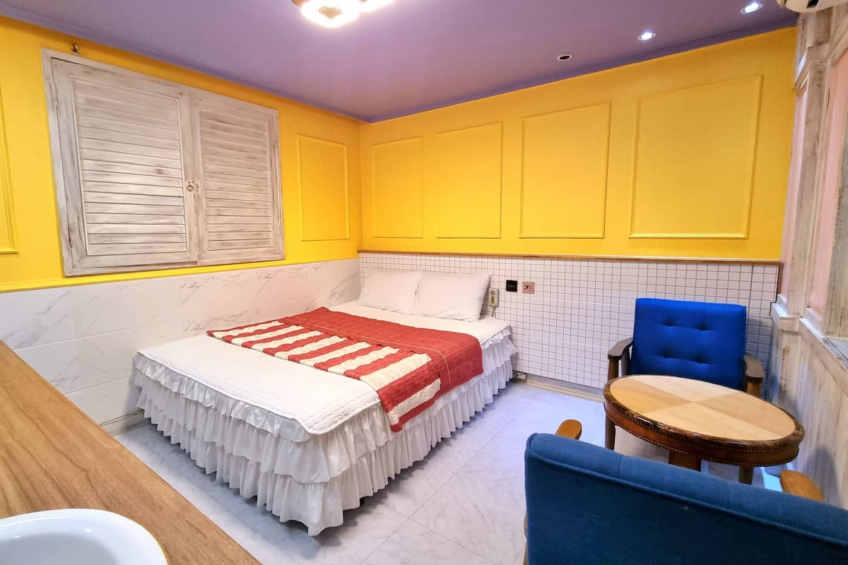 Um quarto pequeno e colorido, com uma cama, uma cadeira e uma mesa de madeira.