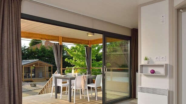 Quarto moderno com porta de vidro deslizante que dá para um deck externo, aquecedor embutido branco e uma pequena estante com objetos decorativos.