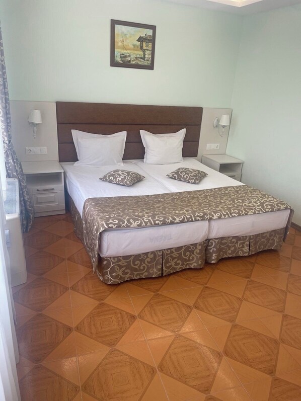 Quarto de hotel com uma cama grande, duas mesas de cabeceira, uma luminária na parede e um quadro sobre a cama.
