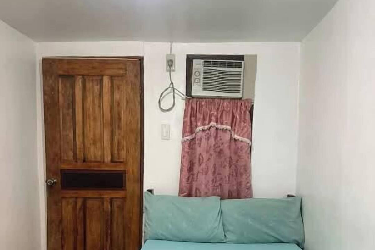 Um quarto com porta de madeira, cama com colchão verde e travesseiro rosa.