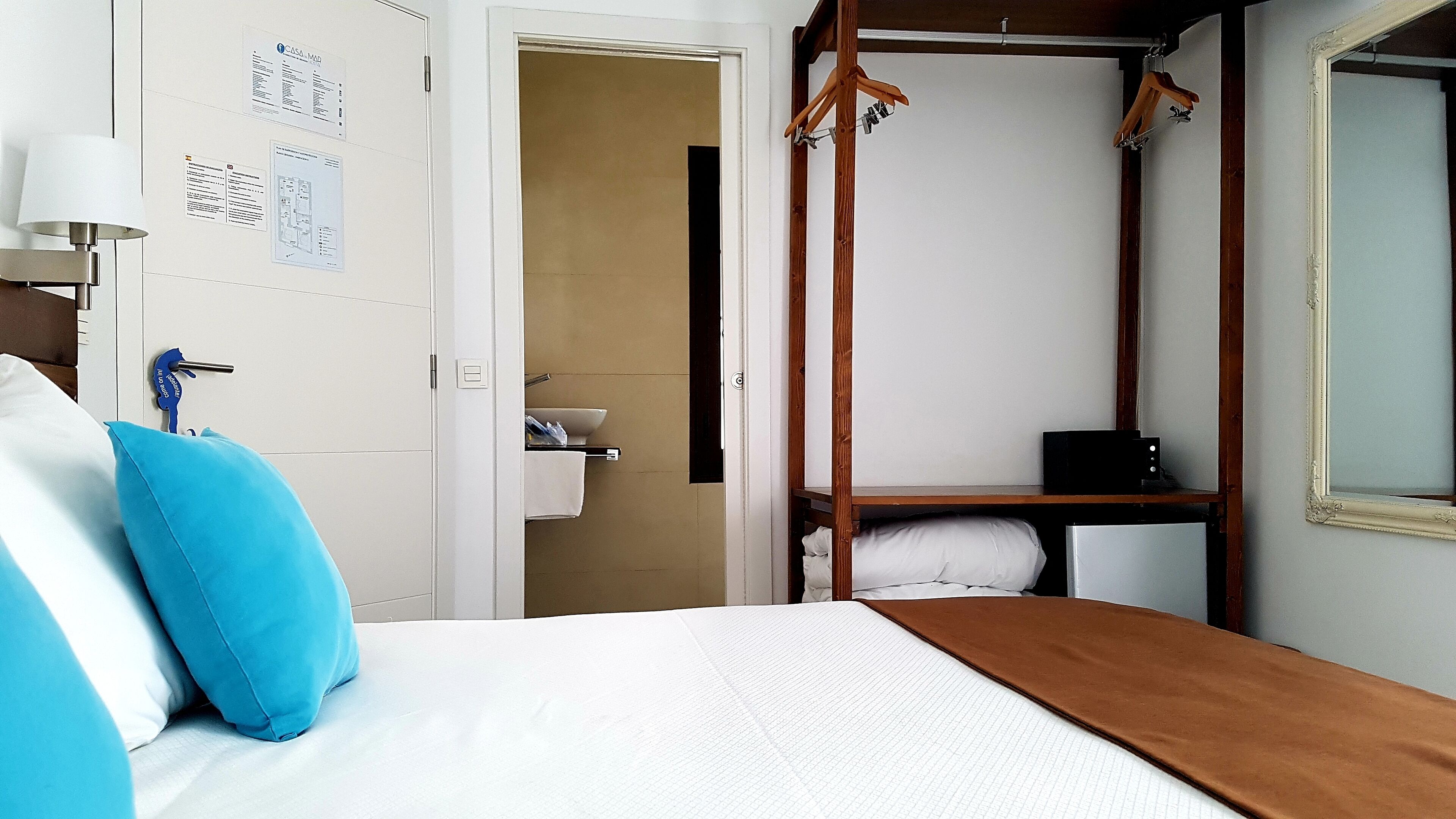Quarto de hotel com cama, mesa de cabeceira de madeira, cadeira de balanço de madeira, espelho e porta para um banheiro.
