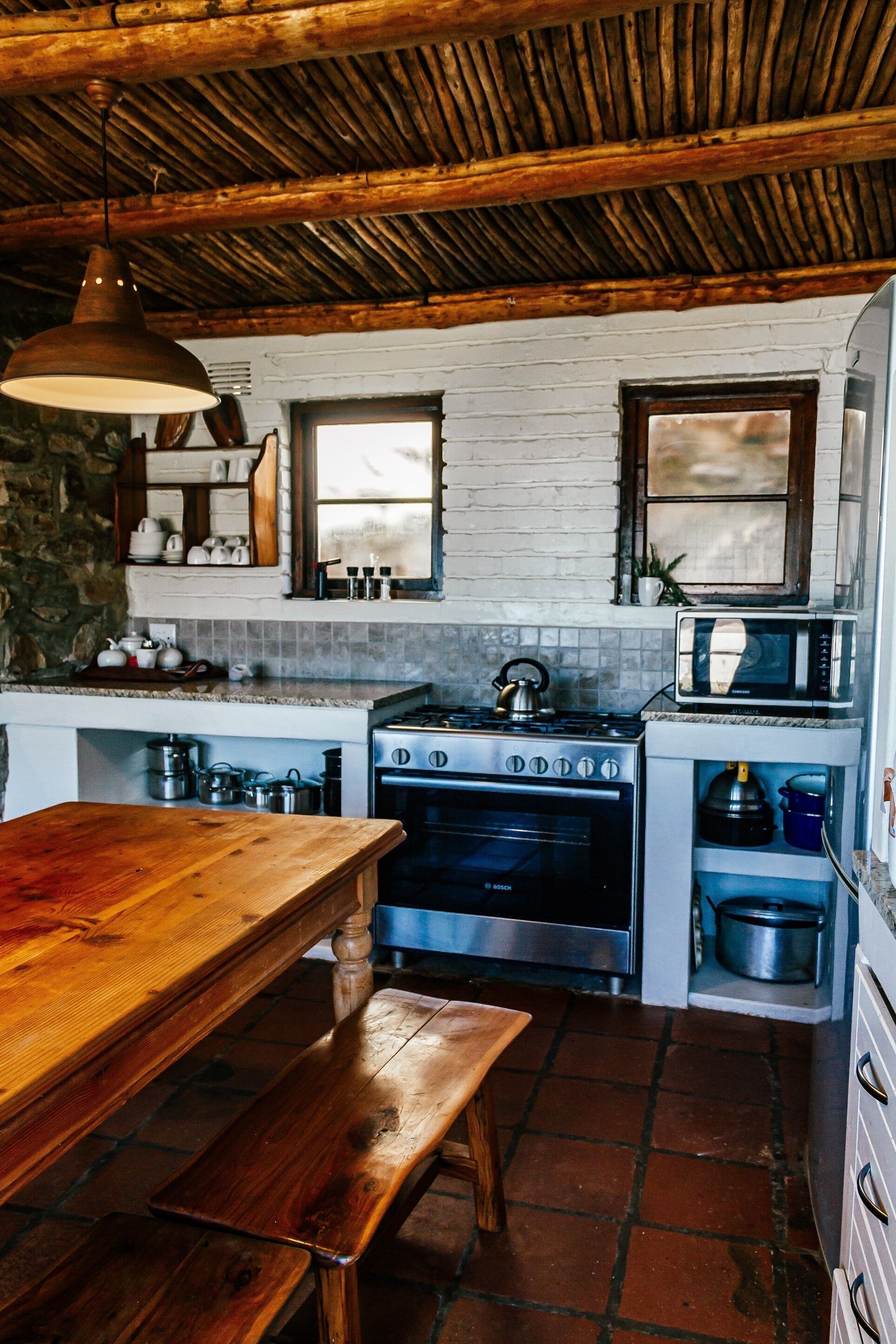 Cozinha rústica com mesa e banco de madeira, fogão e micro-ondas.