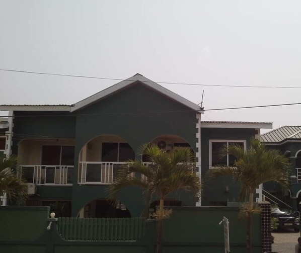 Um edifício de dois andares com fachada verde, várias varandas e uma escadaria que leva ao andar superior.