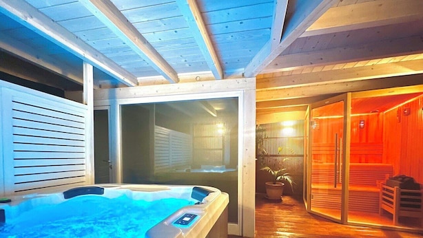 Uma banheira de hidromassagem com painel de controle, piso de madeira e porta de vidro que dá acesso a uma área de sauna.