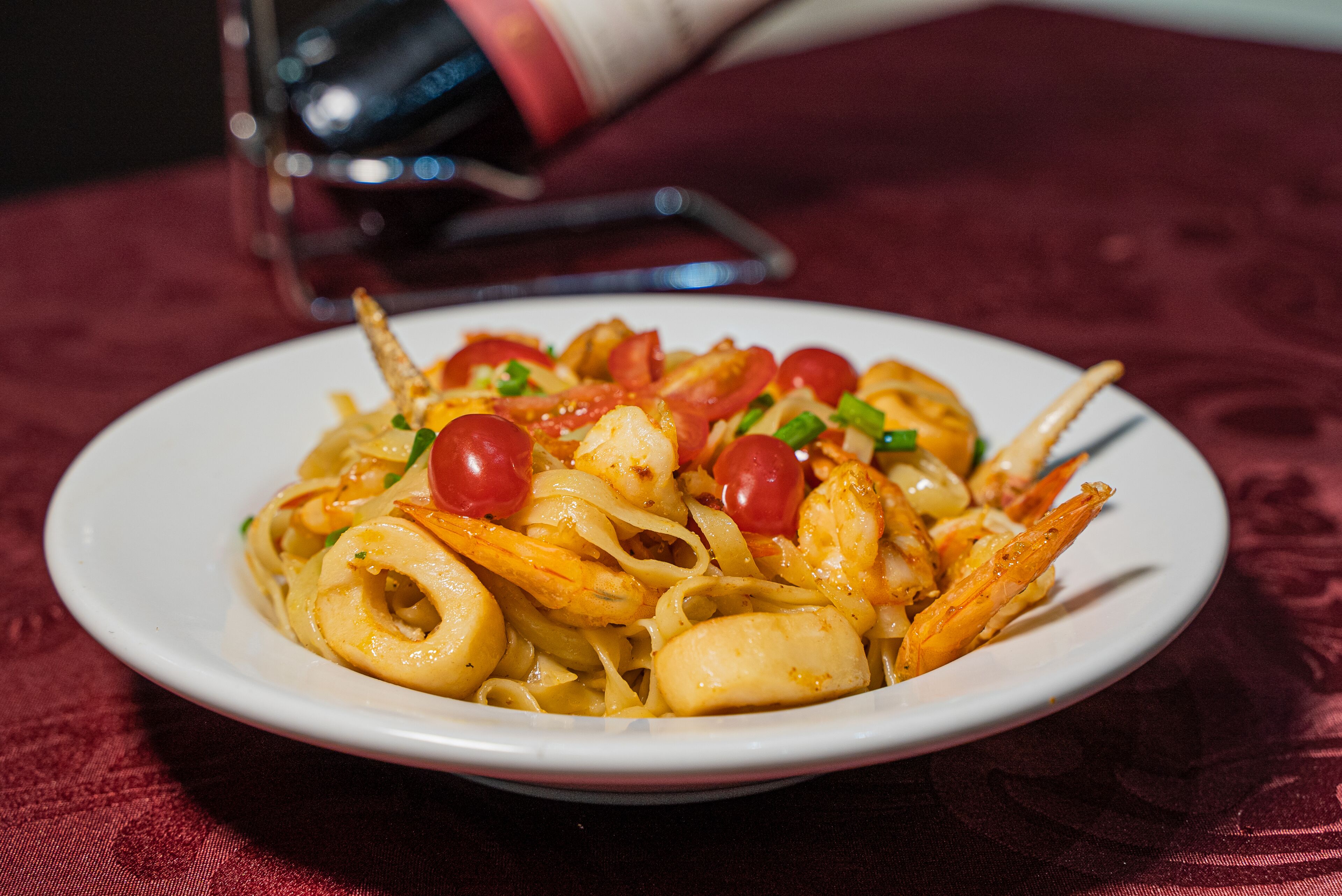 Um prato de massa com camarão, tomate cereja e cebolinha.
