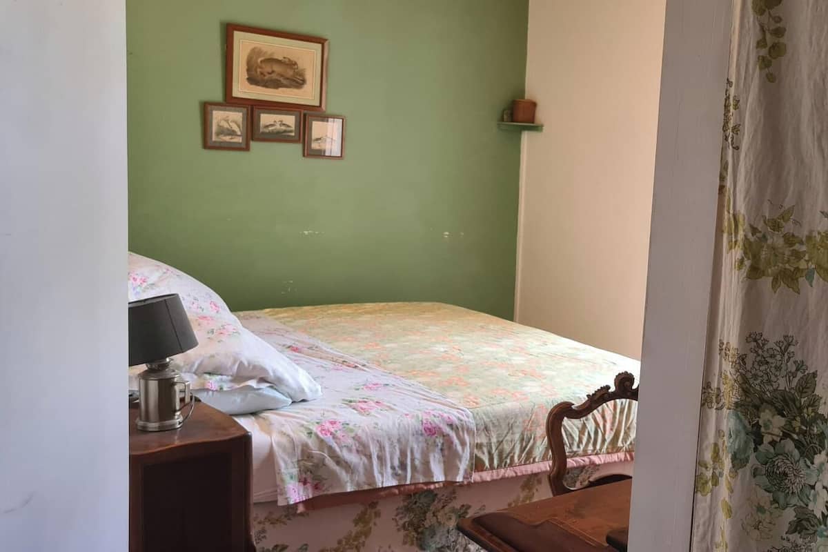 Um quarto com uma cama, uma mesa de cabeceira com abajur, e uma parede com quadros.