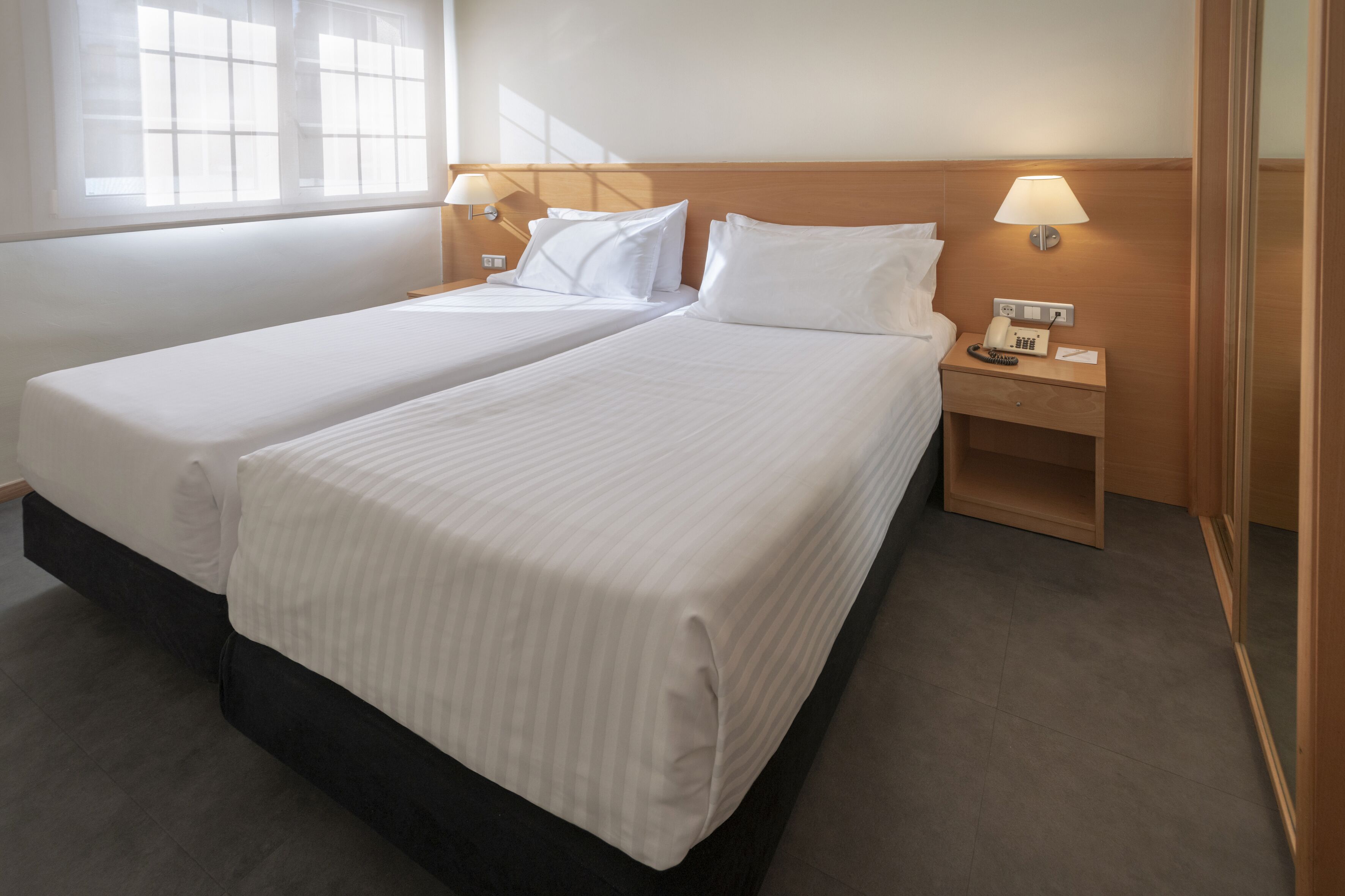 Quarto de hotel com duas camas, uma mesa de cabeceira com abajur e telefone.