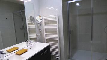 Um banheiro moderno com pia branca, duas espelhos, box de vidro e porta-toalhas.