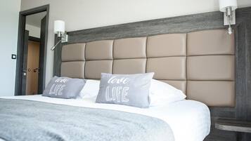 Cama bem arrumada com duas almofadas, um cobertor cinza e cabeceira com luminária.