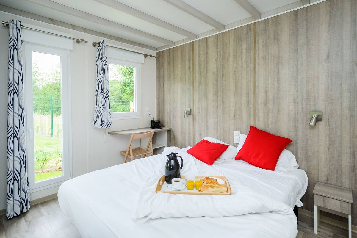 Quarto com cama, bandeja de café da manhã, cafeteira e vista para o verde lá fora.
