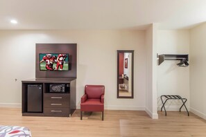 Quarto de hotel com televisão de tela plana na parede, uma cadeira vermelha, uma mesinha com espelho e um porta-roupas.