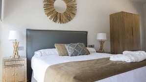Uma cama bem arrumada com cabeceira cinza, duas luminárias de apoio e um guarda-roupa de madeira grande.