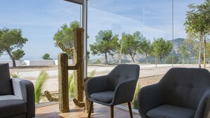 Uma sala de estar moderna com uma grande janela que oferece vista para uma paisagem deslumbrante, incluindo árvores e o mar ao longe.