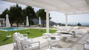 Uma área externa coberta com móveis brancos, piscina e vista para a paisagem.