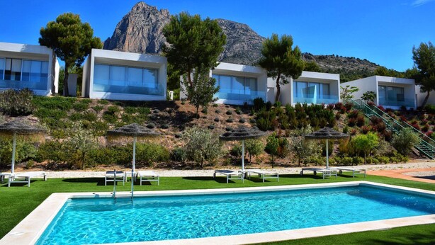 Um hotel moderno com piscina, rodeado por vegetação exuberante e montanhas ao fundo.
