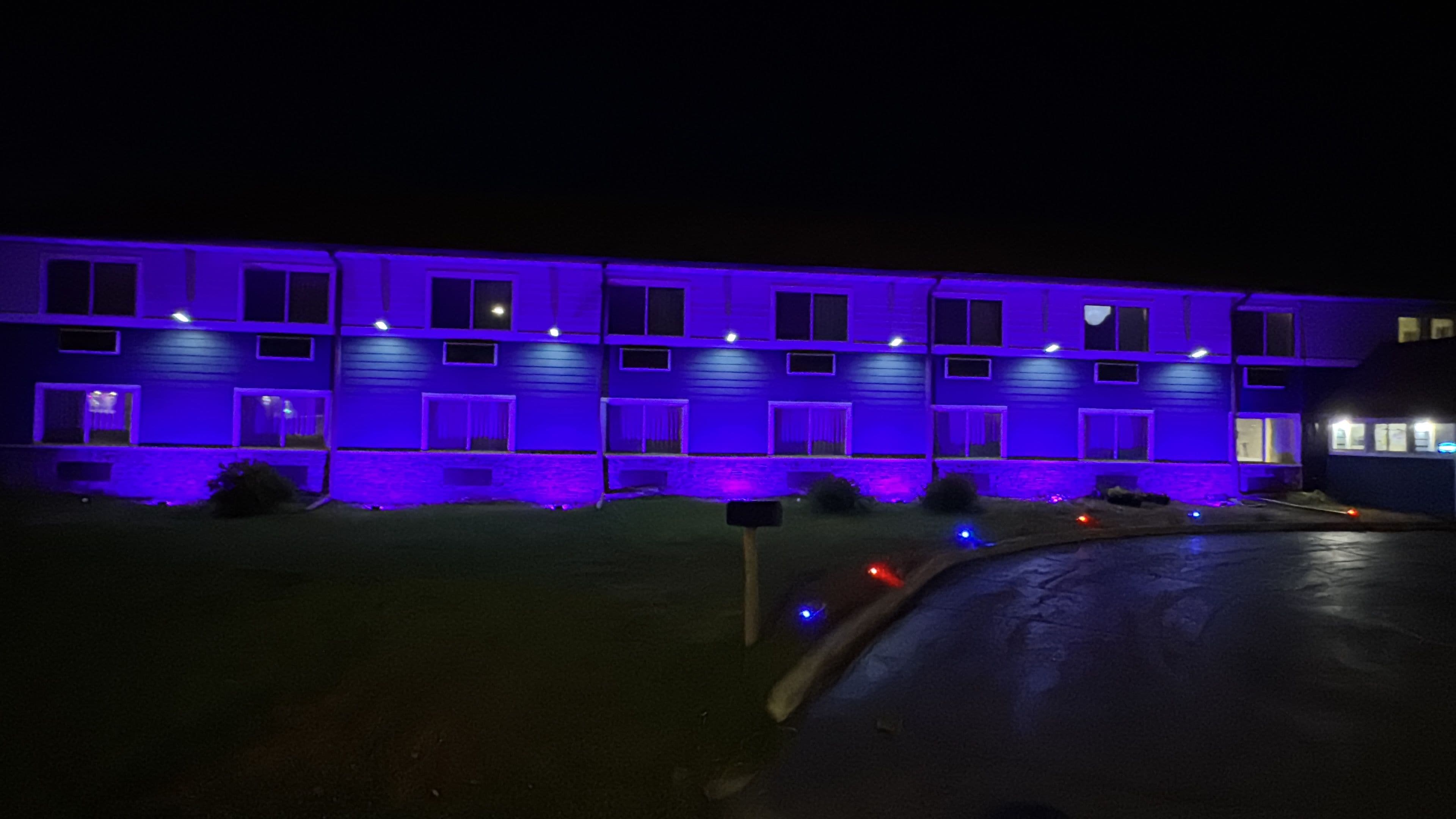 Edifício de vários andares com telhado plano, iluminado por luzes roxas.