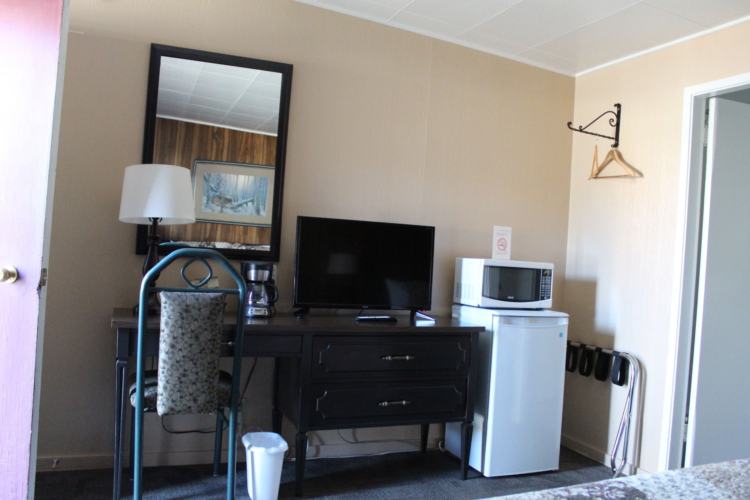 Quarto de hotel com escrivaninha, televisão, micro-ondas, mini-geladeira, cadeira, cabideiro e porta.